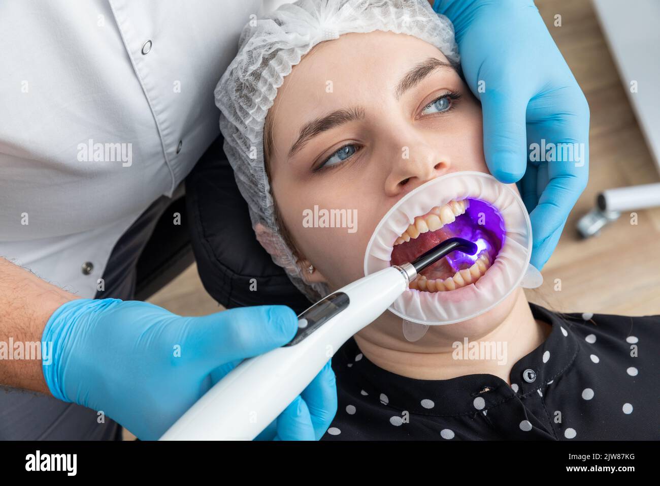 Closeup view of dentist using dental curing UV lamp on teeth of patient ...