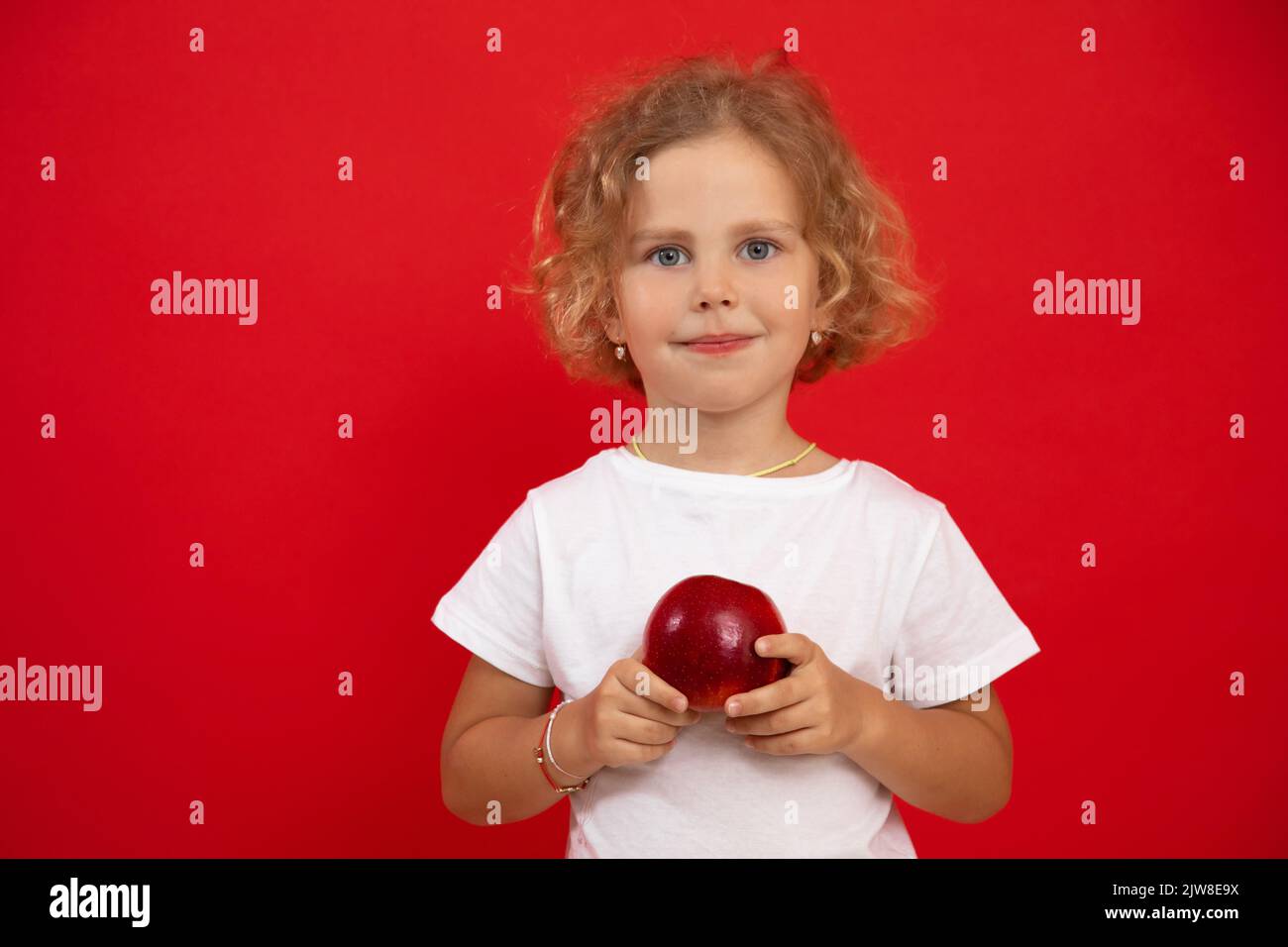 Small little expressive, positive curly blonde girl holding red juice ...