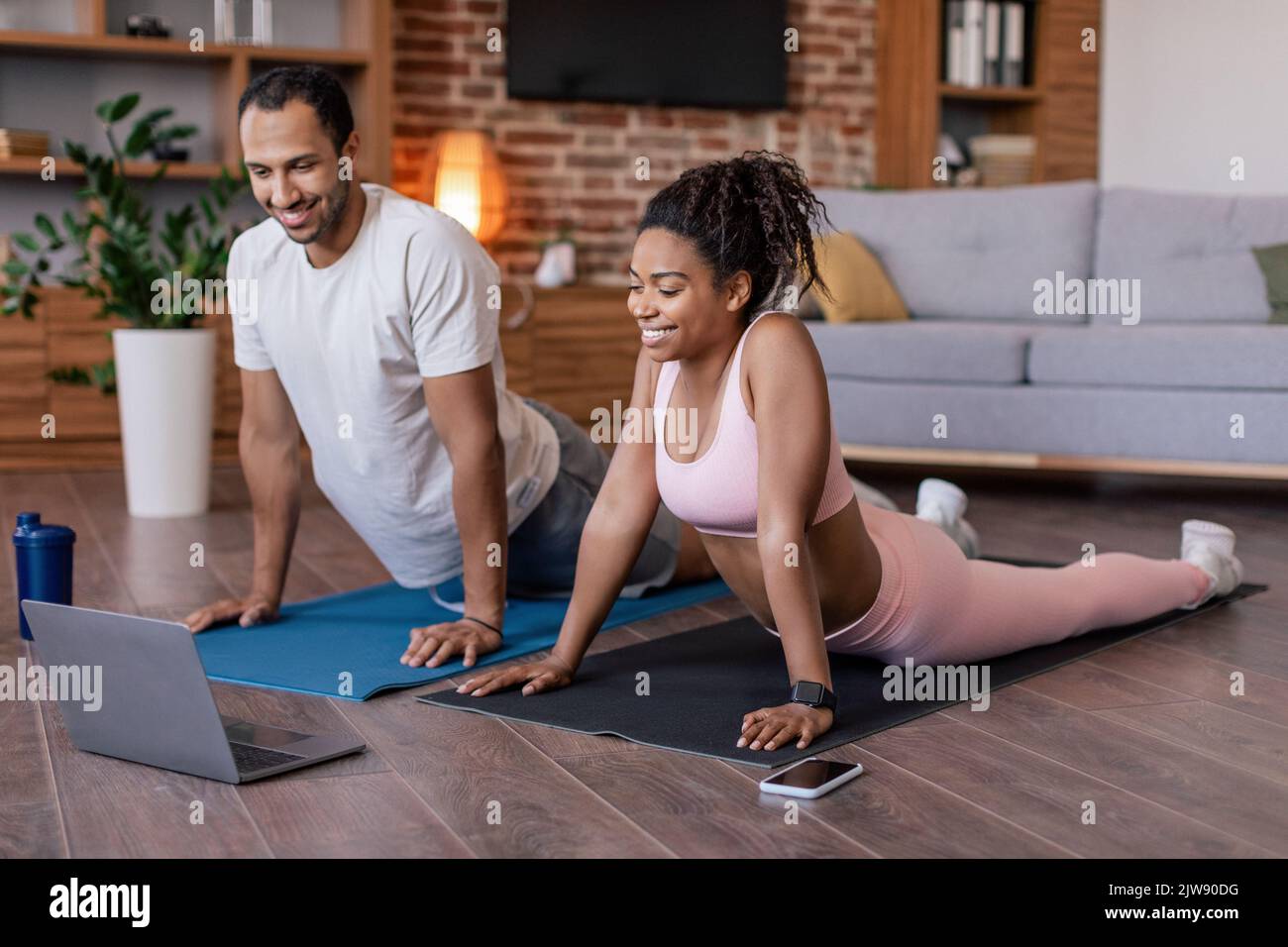 Glad young black couple in sportswear do stretching or practicing yoga ...