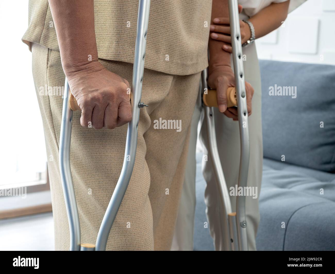 Closeup elderly woman's hands holding on crutches standing in living ...