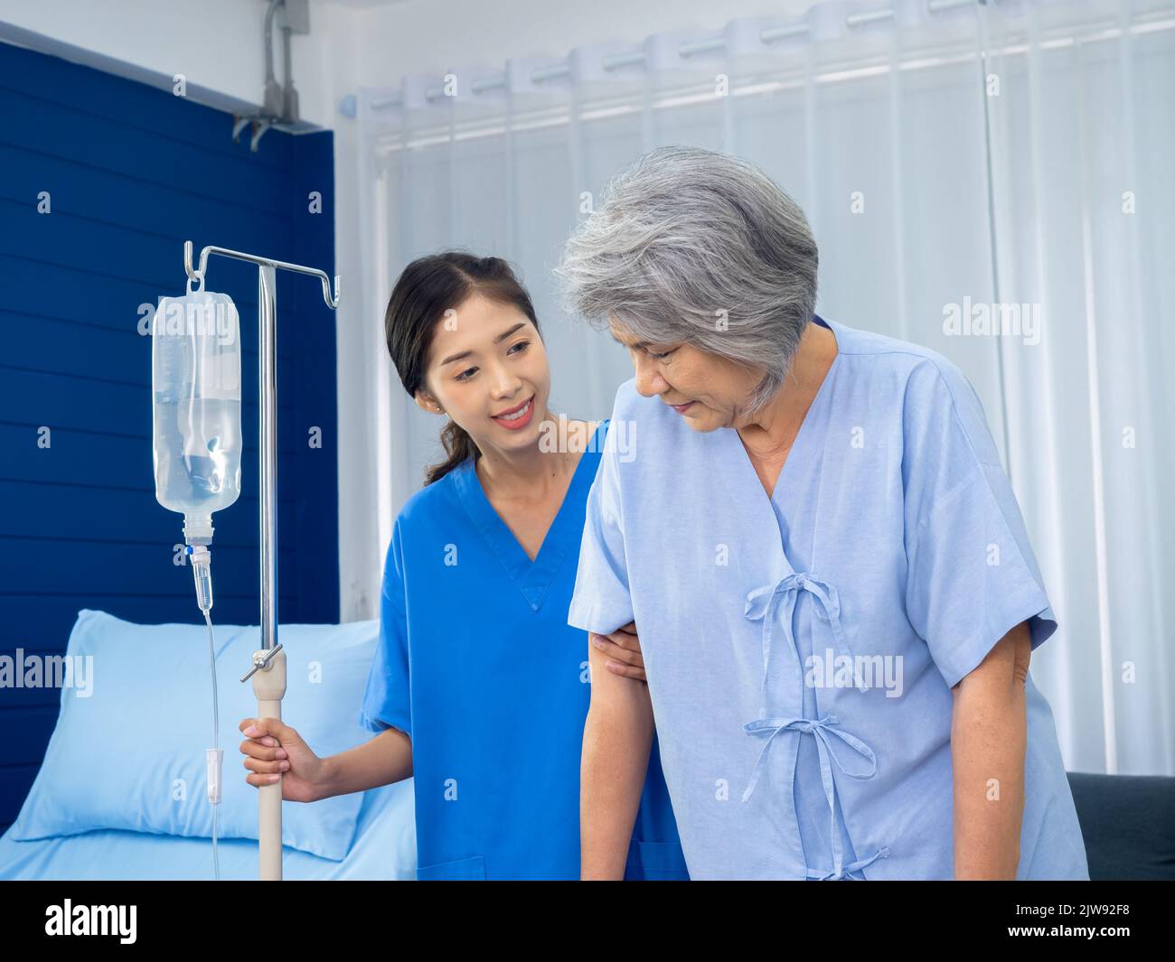 Elderly Asian woman patient trying to walk on walking frame held and ...