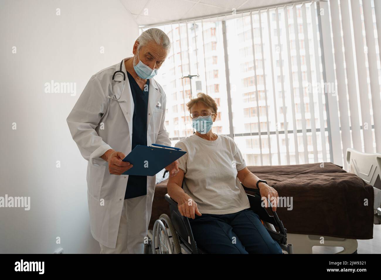 Doctor in mask explaining to a sick patient in a wheelchair the details ...