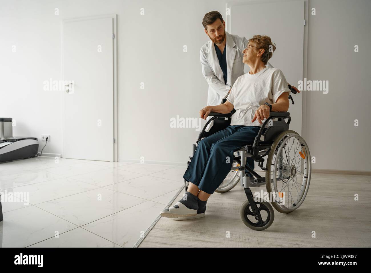Professional male doctor carrying female patient on wheelchair in ...