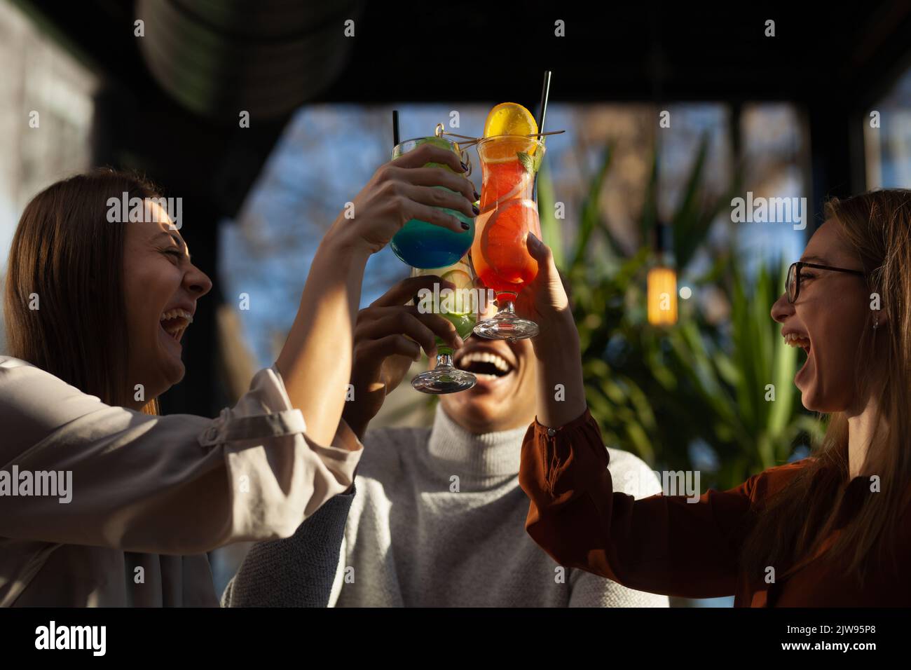 Three multiracial friends in a bar cheering. After work party with ...