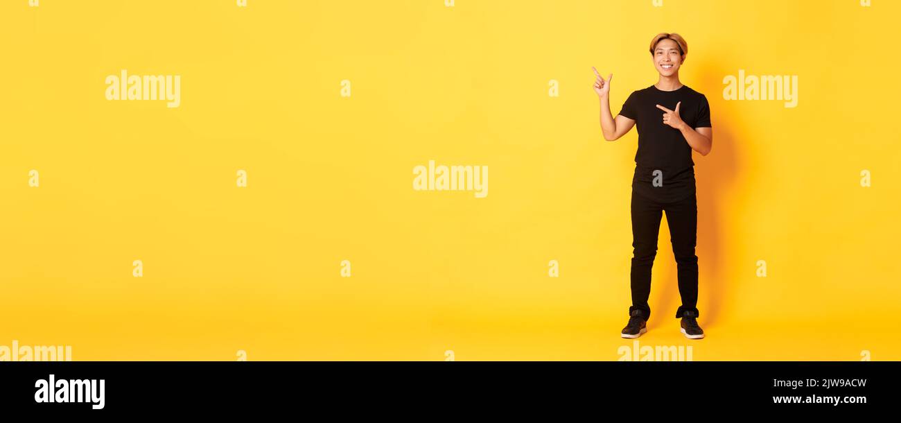 Full-length of smiling attractive korean guy pointing fingers left ...