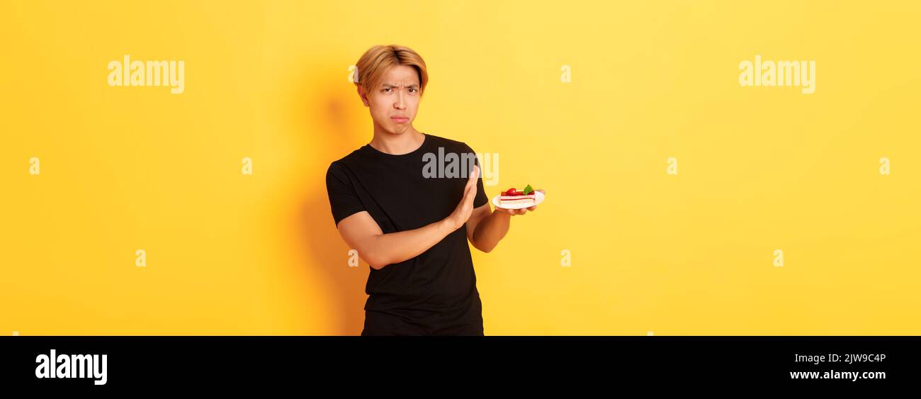Portrait of disgusted and upset young asian guy refuse eating cake ...