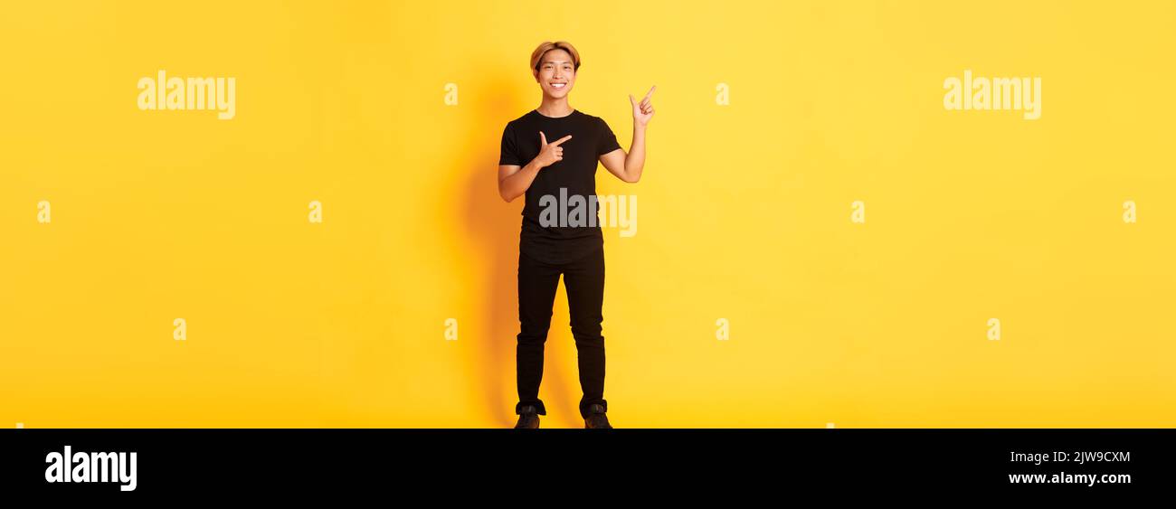 Full-length of smiling attractive korean guy pointing fingers left ...