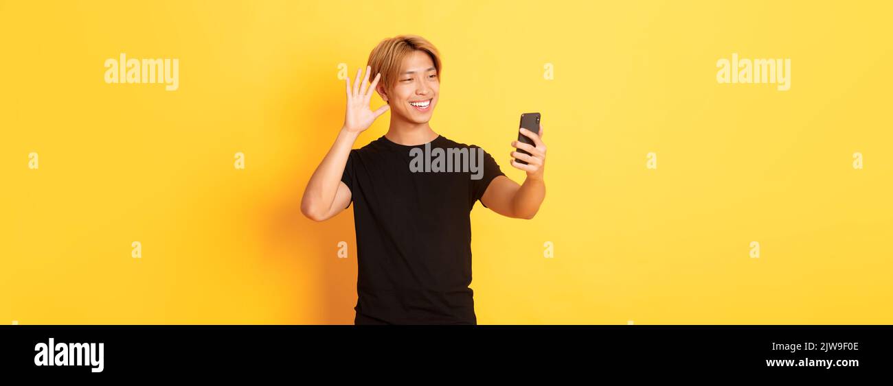 Portrait of friendly handsome asian man, smiling and waving hand at ...