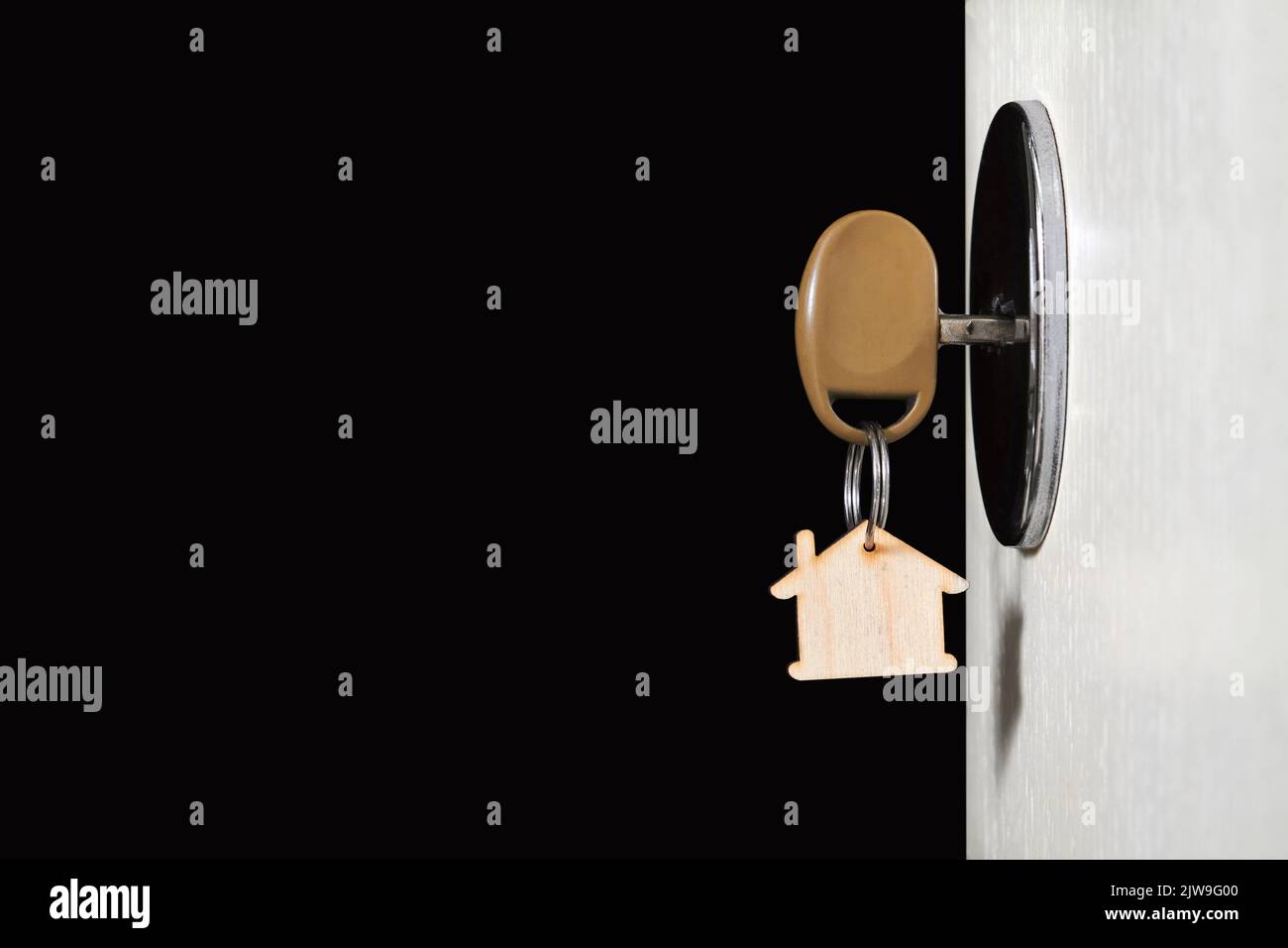 Key with a trinket in the form of a house in the door lock of an open ...