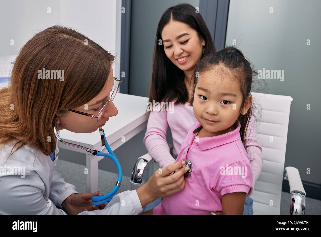 Pediatrician check-up child's lungs and heart using stethoscope. Little Asian girl sitting on ...