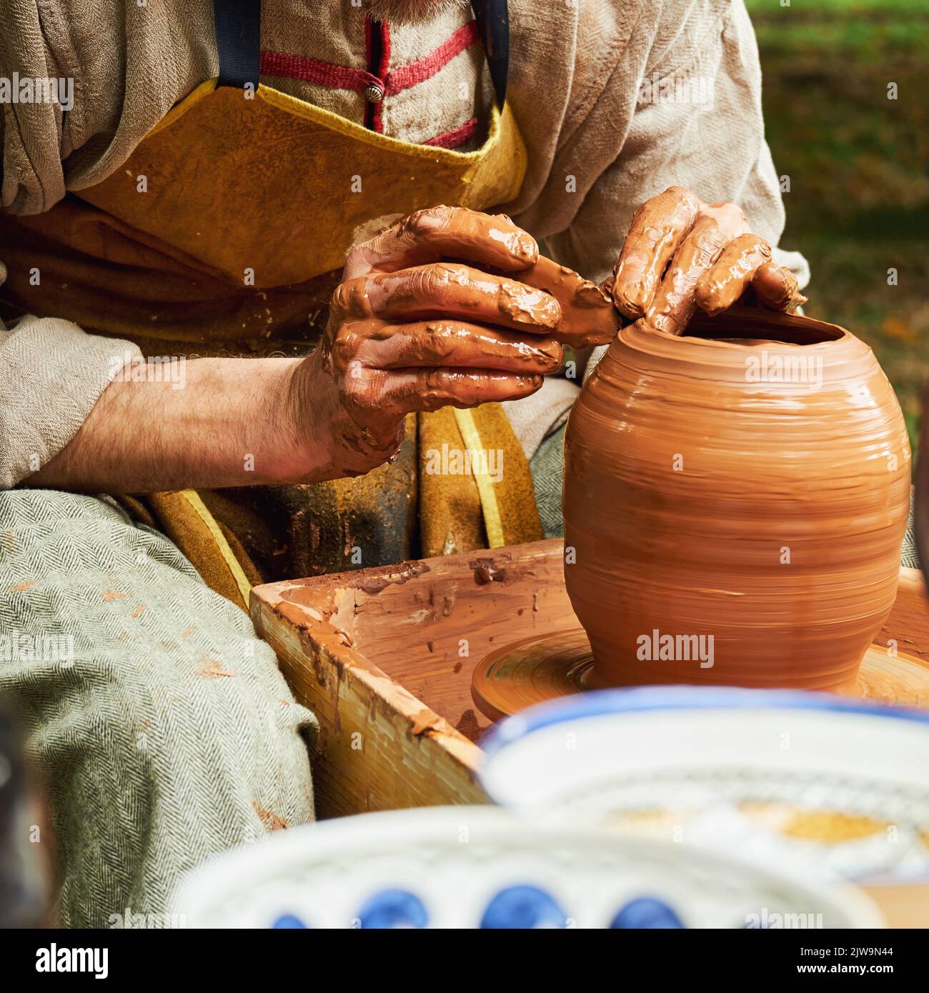 A man in old medieval Byzantine clothes sits behind a vintage potter's ...