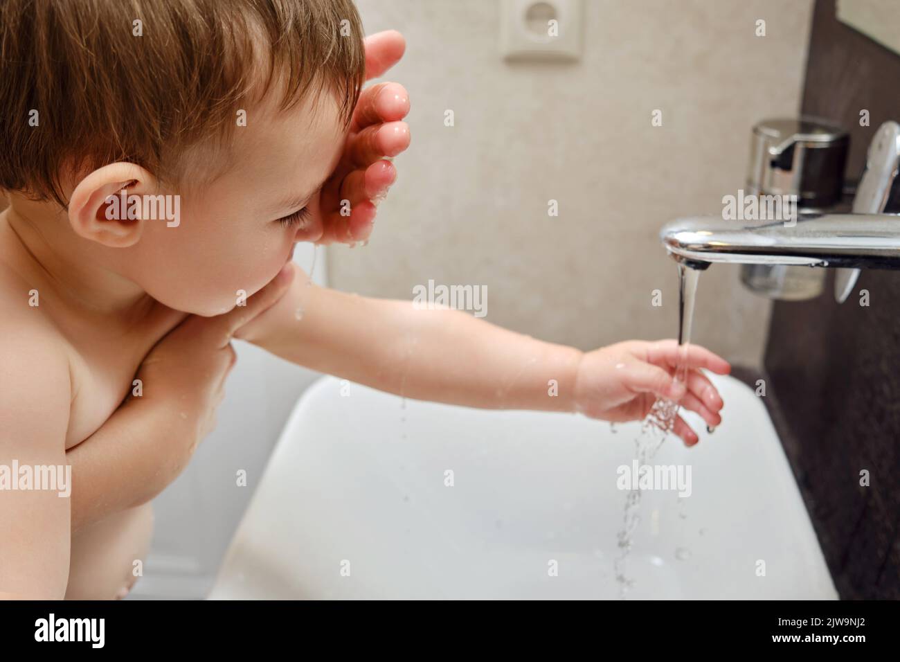 Woman mother washes face of happy toddler baby in sink with faucet. Mom ...