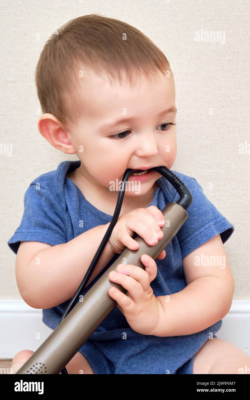 Child boy chewing on the electric wire of a curling iron. Toddler baby ...