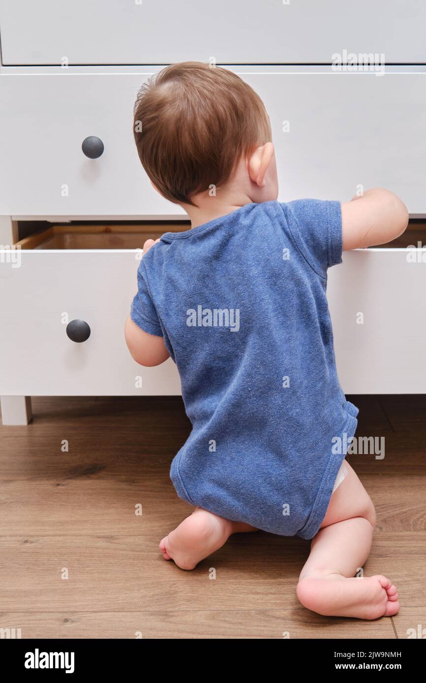 Toddler baby opens a chest of drawers. Child boy reaches into an open ...