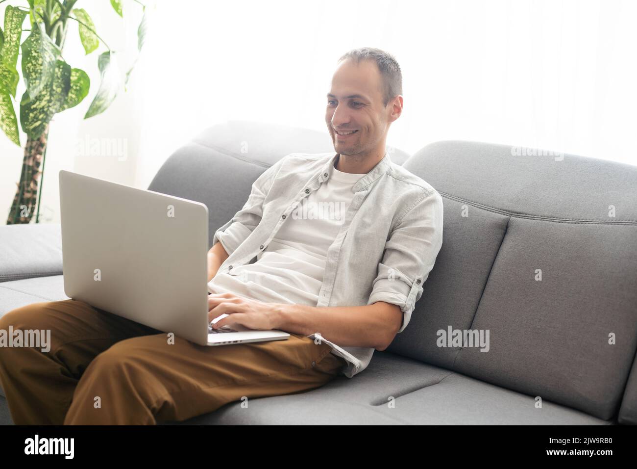 Young male tech user relaxing on sofa holding laptop computer mock up ...