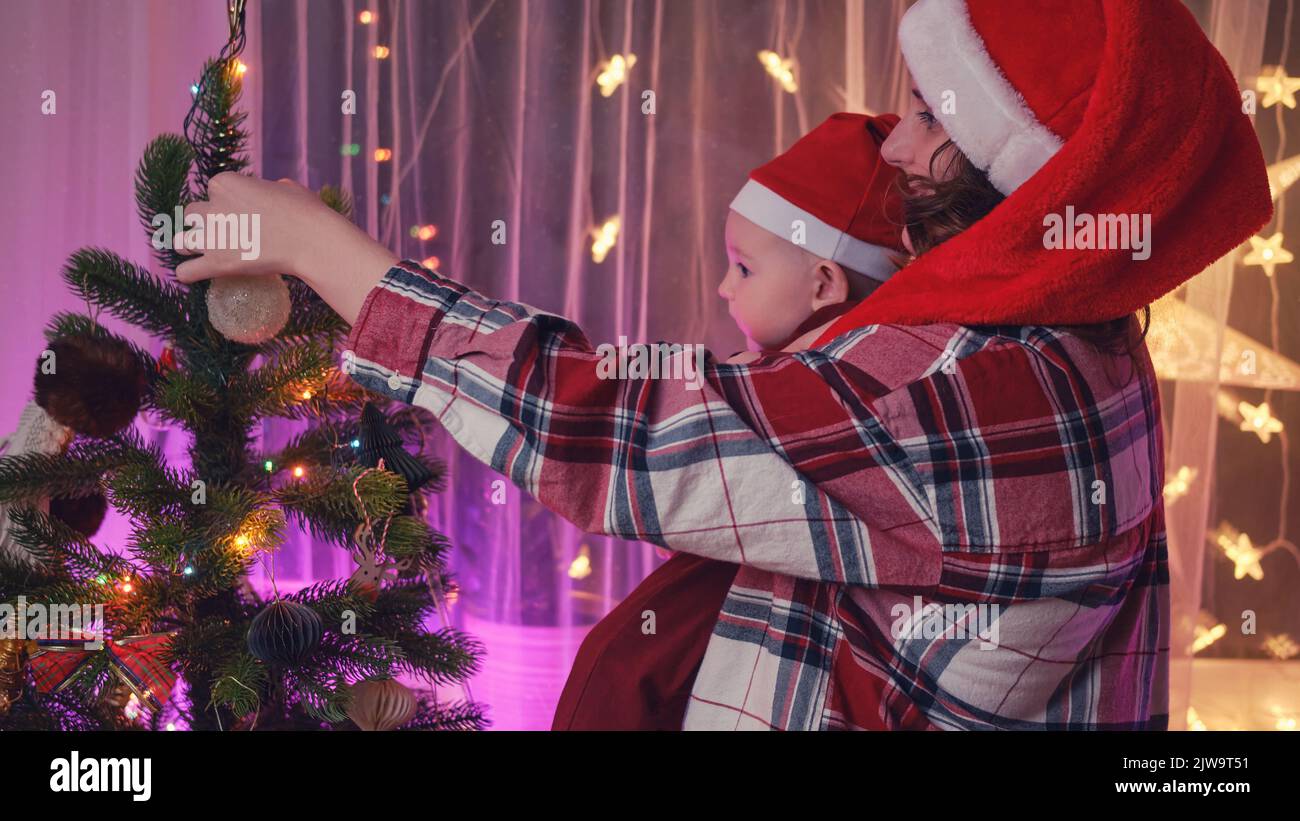 Baby boy toddler with his mother decorate the family Christmas tree ...
