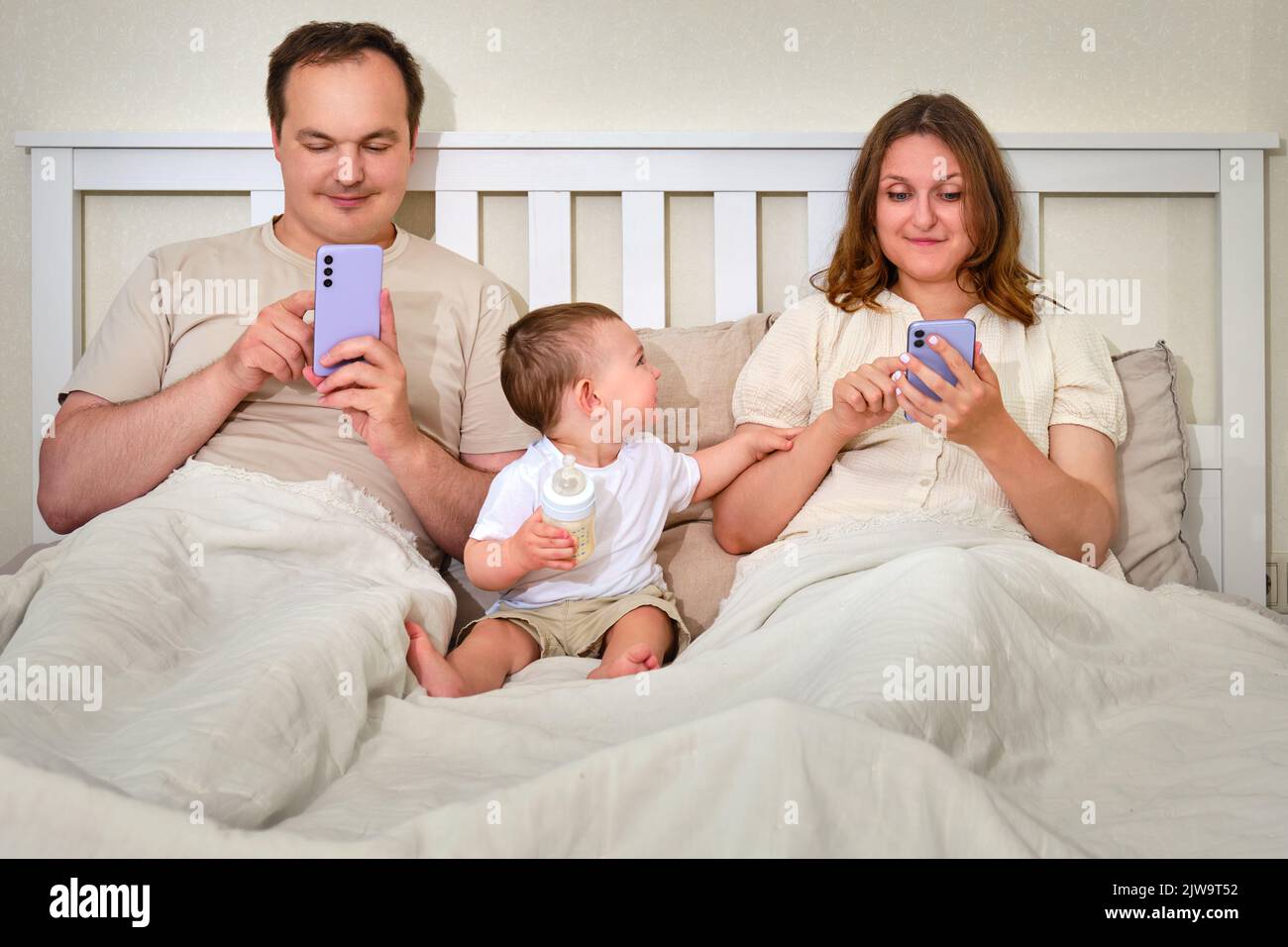 Happy man and woman with toddler baby looking in a mobile phone. Father ...