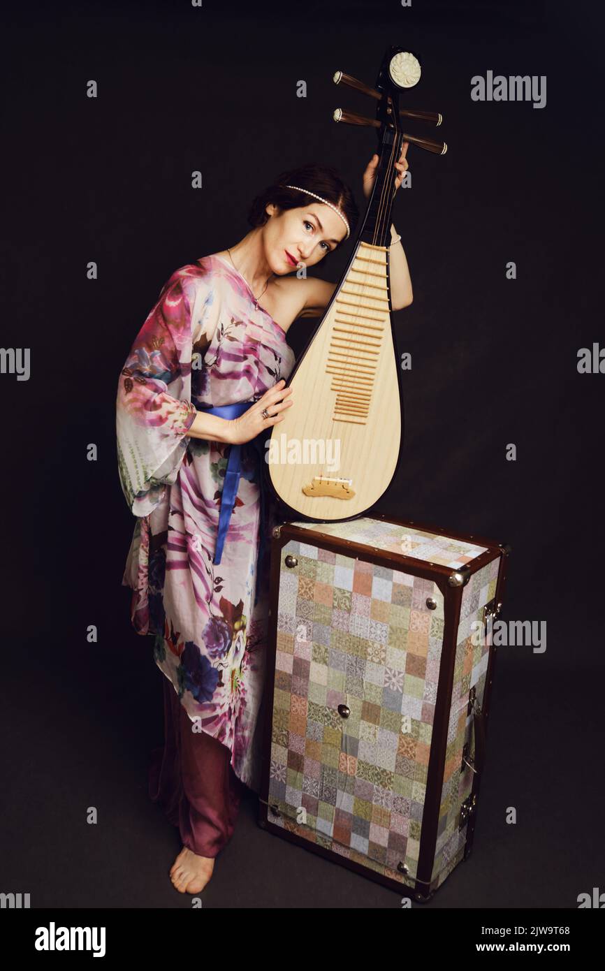 A happy female musician in Asian clothes on a studio black background ...