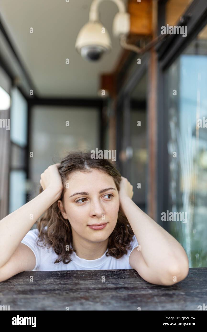 A smiling brunette girl in a white T-shirt, blue jeans sits at a wooden ...