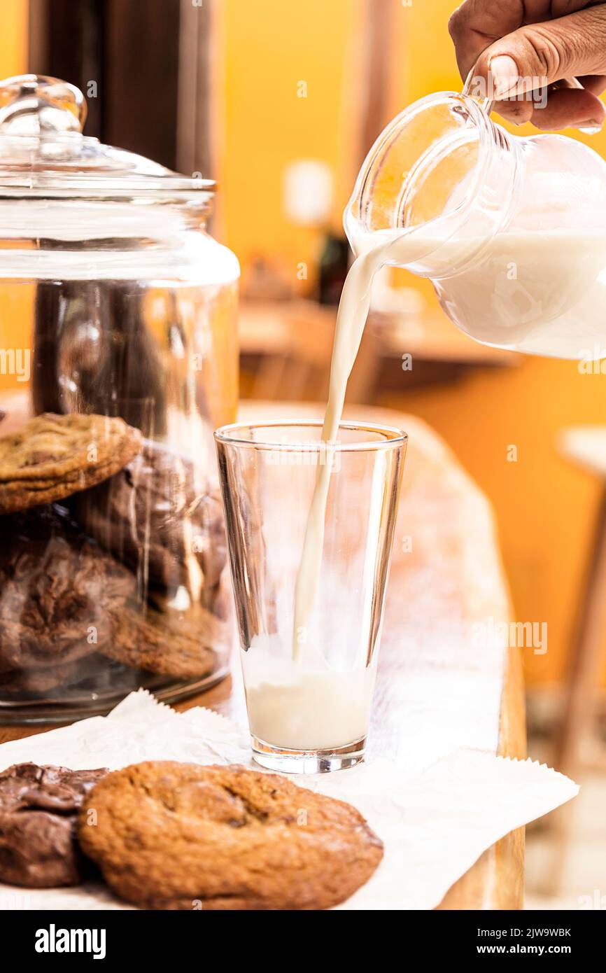 Hand holding a pitcher while pouring milk into a glass tumbler. In the ...