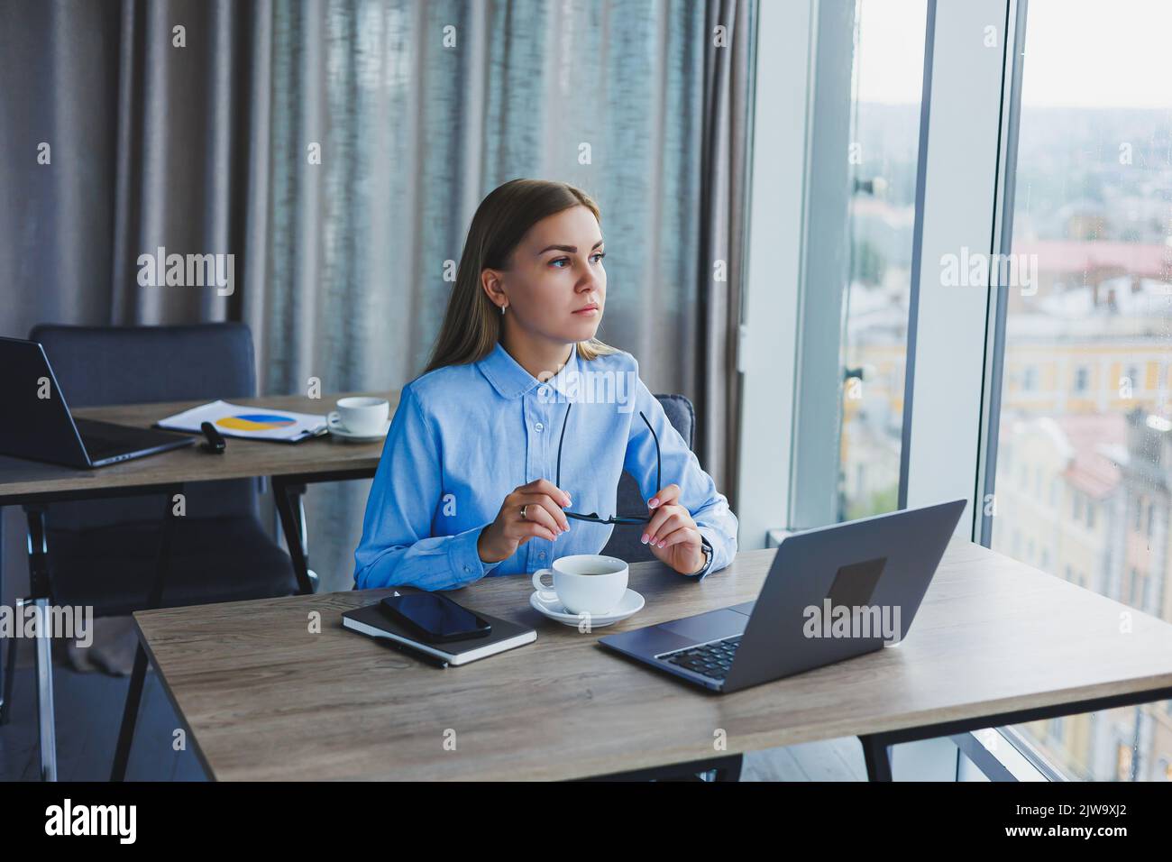 Adult smiling female manager in glasses and formal shirt sits at a desk ...
