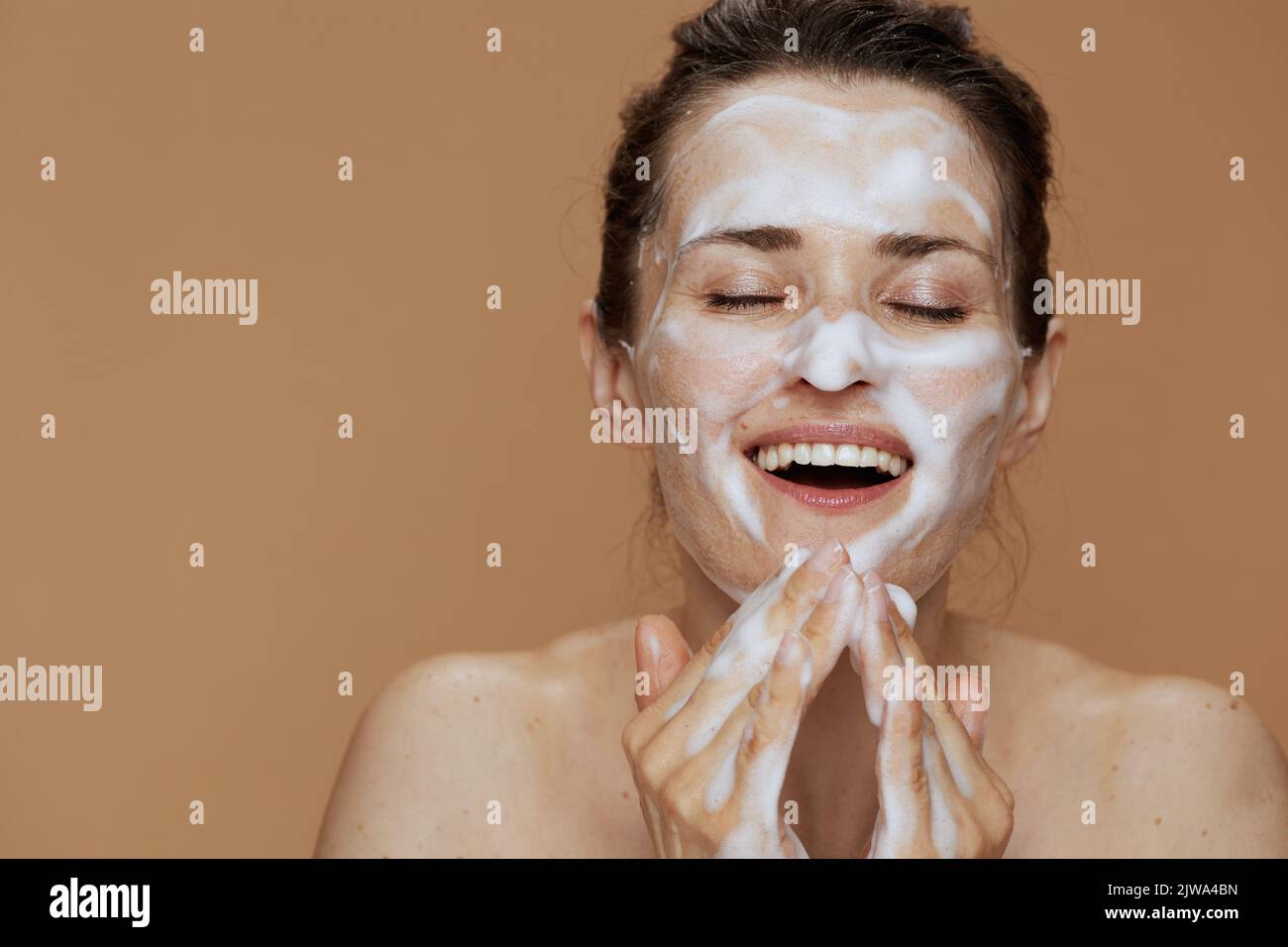 happy young woman with foaming face wash washing face against beige ...