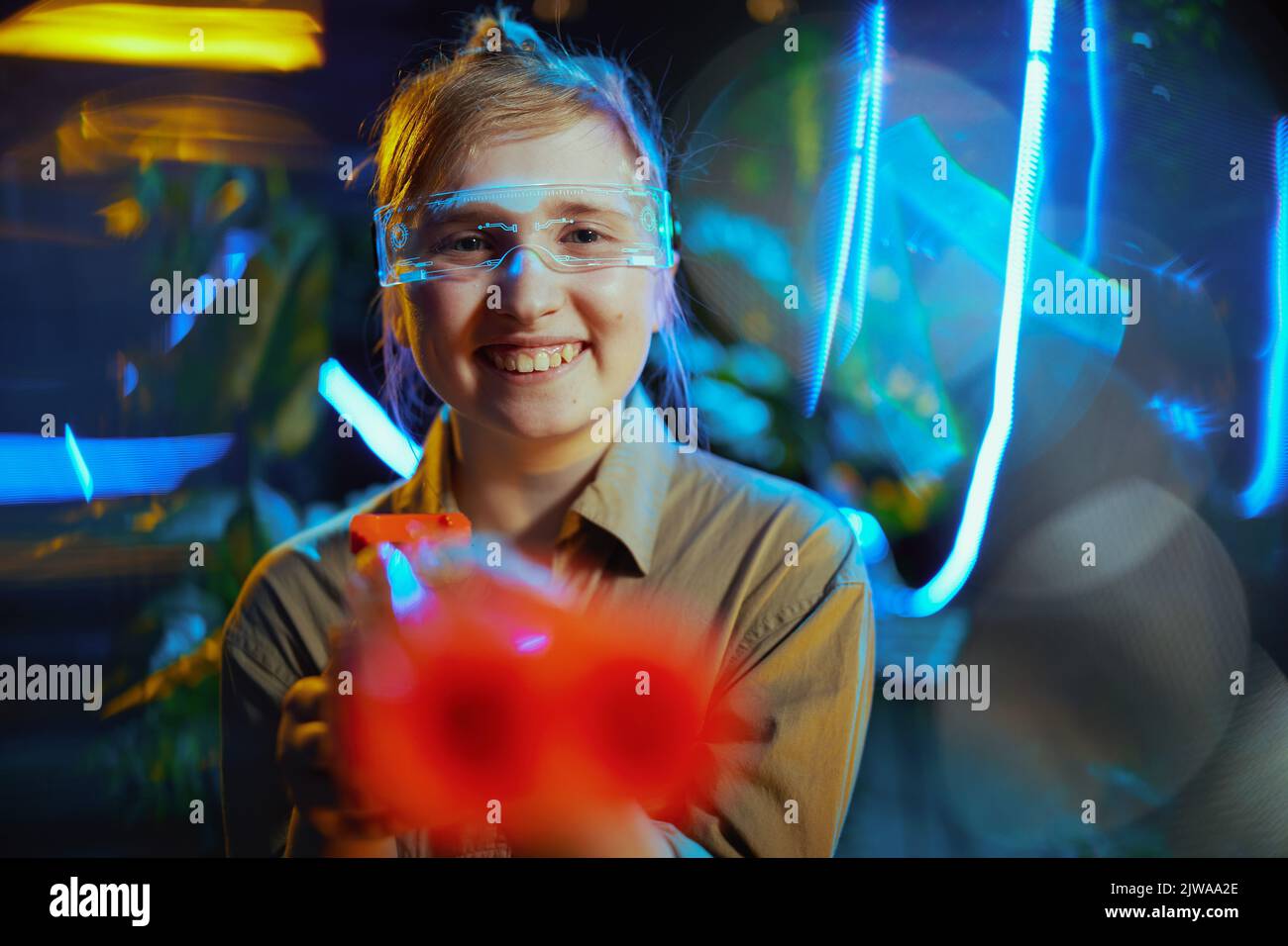 smiling trendy girl with toy gun and futuristic glasses in virtual ...