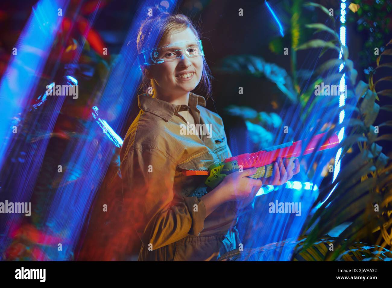 smiling trendy child with toy gun and futuristic glasses in virtual ...