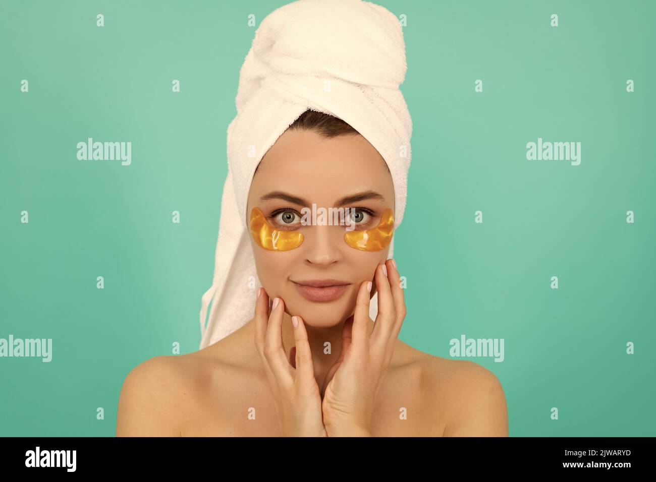 young positive girl has collagen golden eye patches on face with towel ...