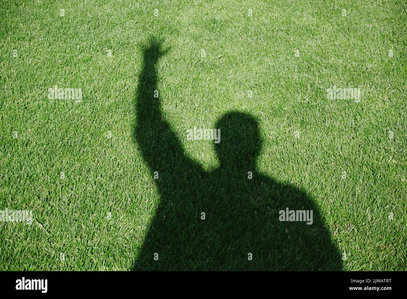 Male hand shadow silhouette with raised hand on green grass lawn ...