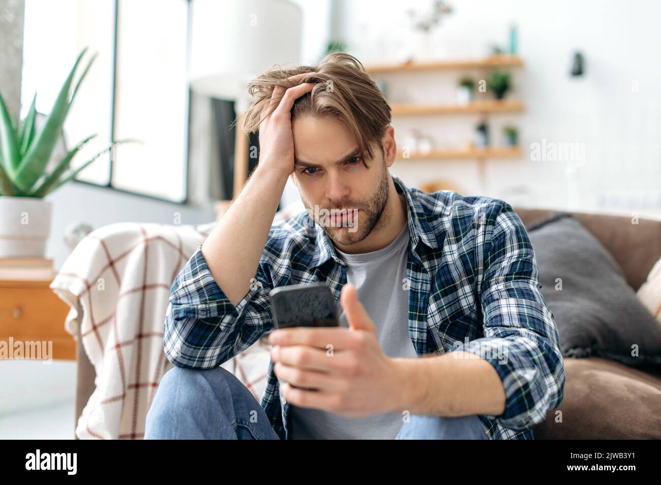 Sad confused upset caucasian young stylish man, sitting on a floor near ...