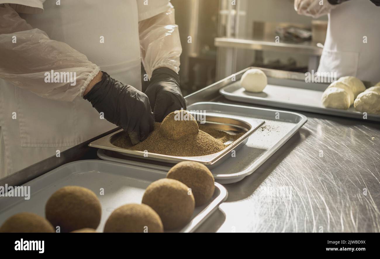 A farmer in black gloves sprinkle black pepper on a cheese ball. The ...