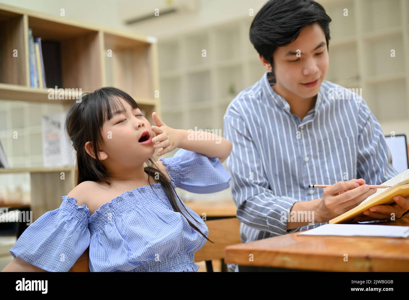 An adorable young Asian girl felling sleepy and yawning while studying ...