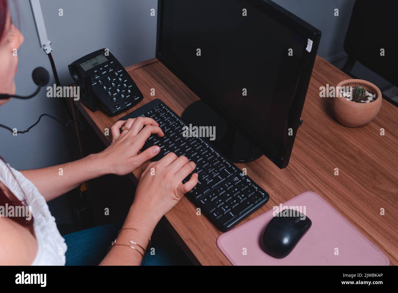 Woman working at a desk in an office with a computer. Red-haired woman ...