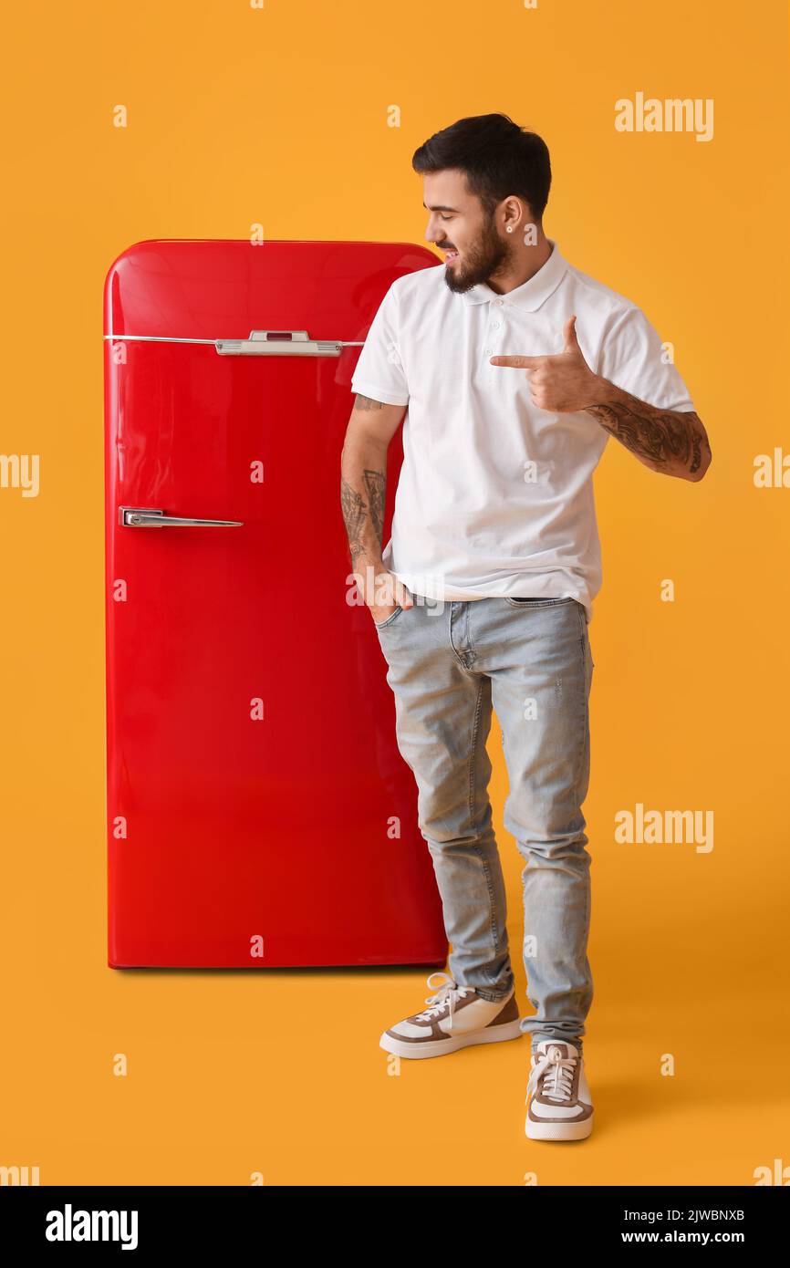 Cool tattooed young man near red fridge on yellow background Stock ...
