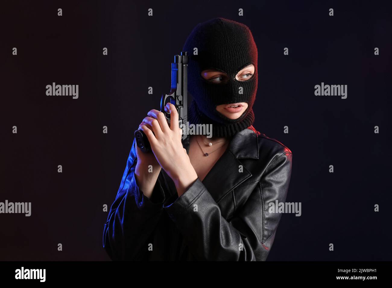 Portrait of young woman in balaclava and leather jacket with gun ...