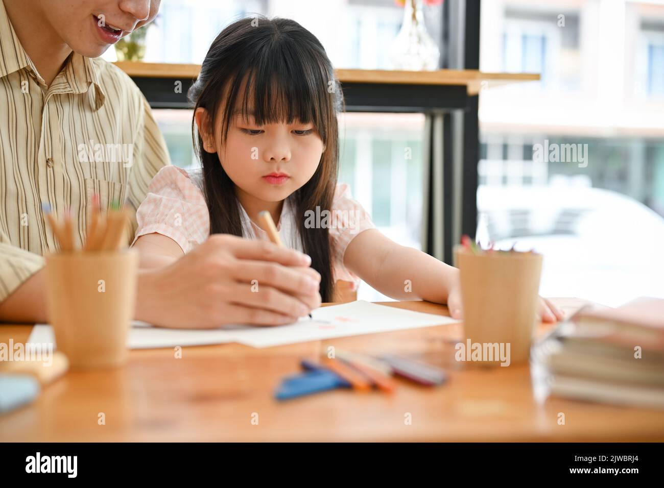 Pretty young Asian girl concentrating doing homework, drawing a cute ...