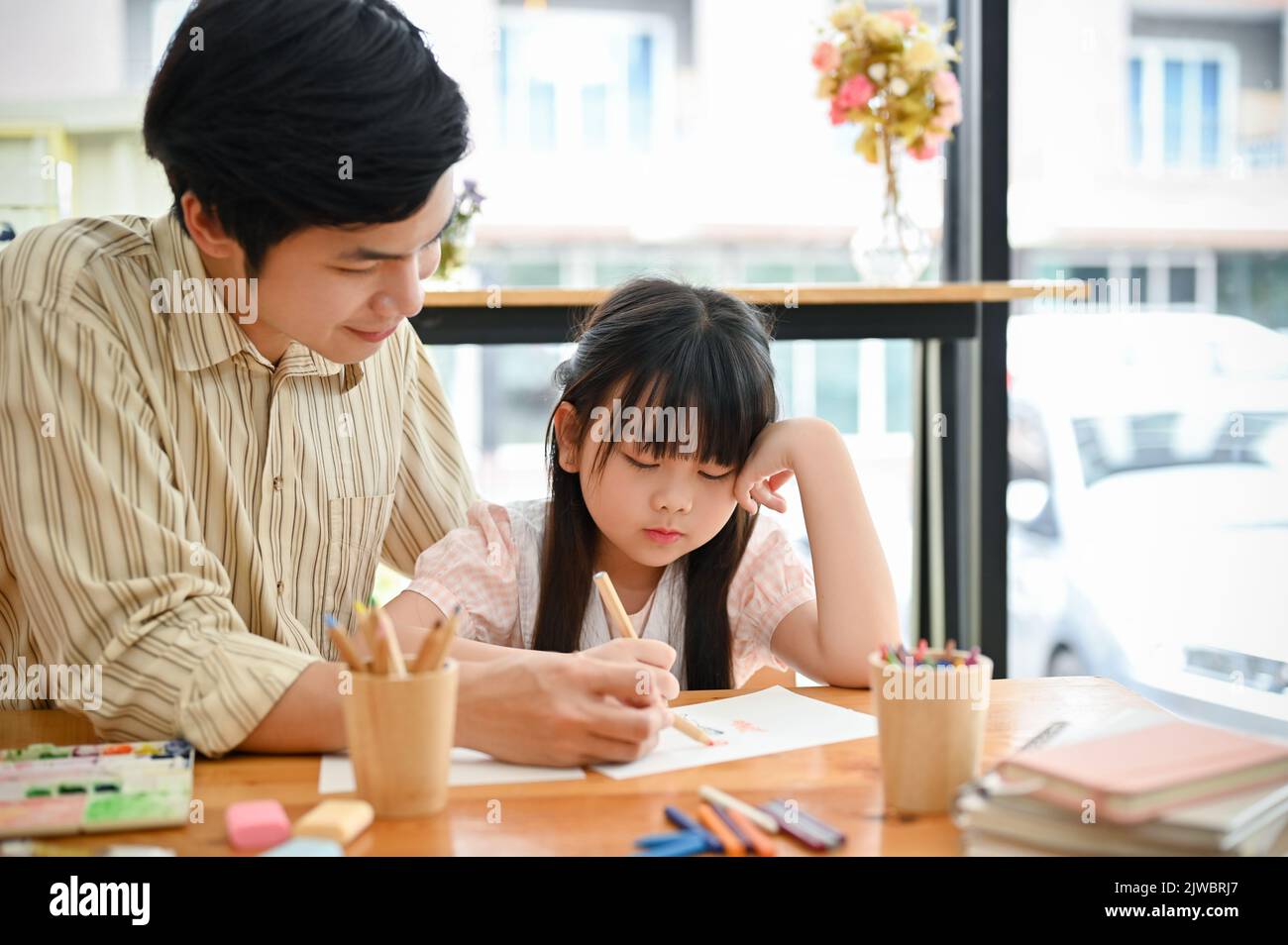 An adorable cute young Asian girl focused doing her art homework. Kind ...
