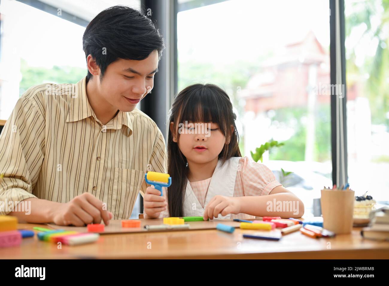 A proud and kind Asian male art teacher is teaching a young girl to ...
