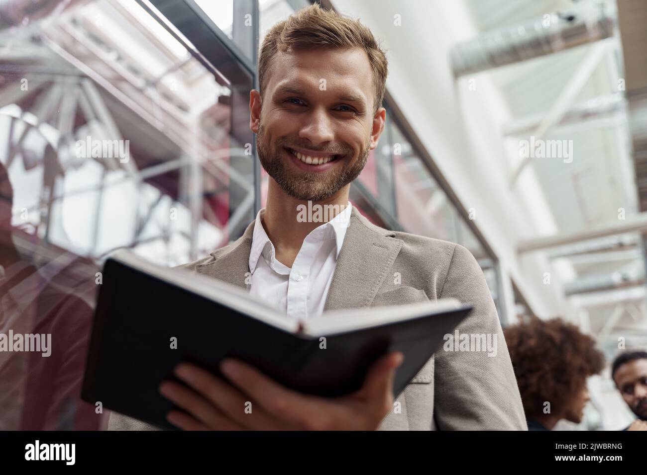 Smiling handsome businessman standing in office and looking at camera ...