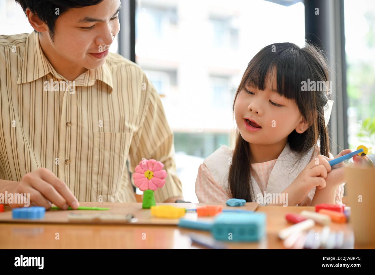 Charming and pretty young Asian girl enjoys playing play dough ...