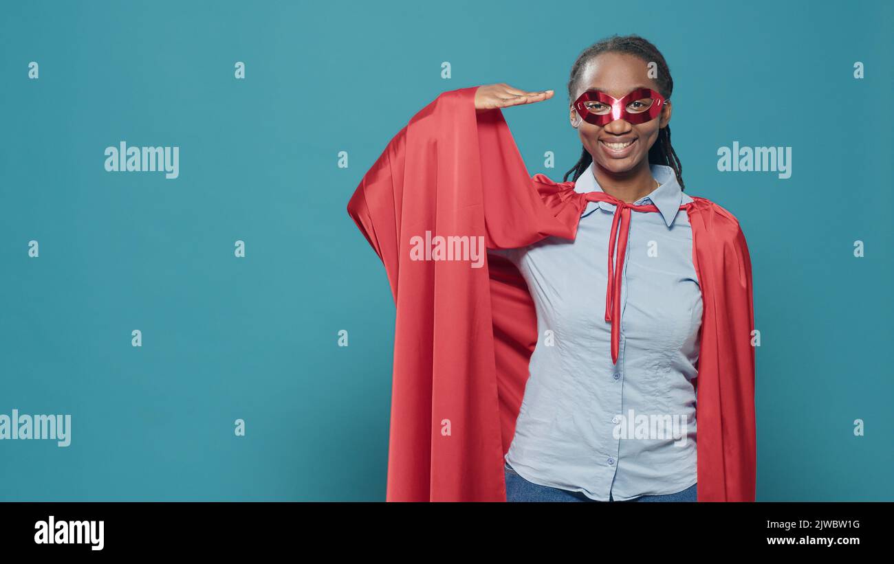 Portrait of superhero with cape and red mask doing army military salute ...
