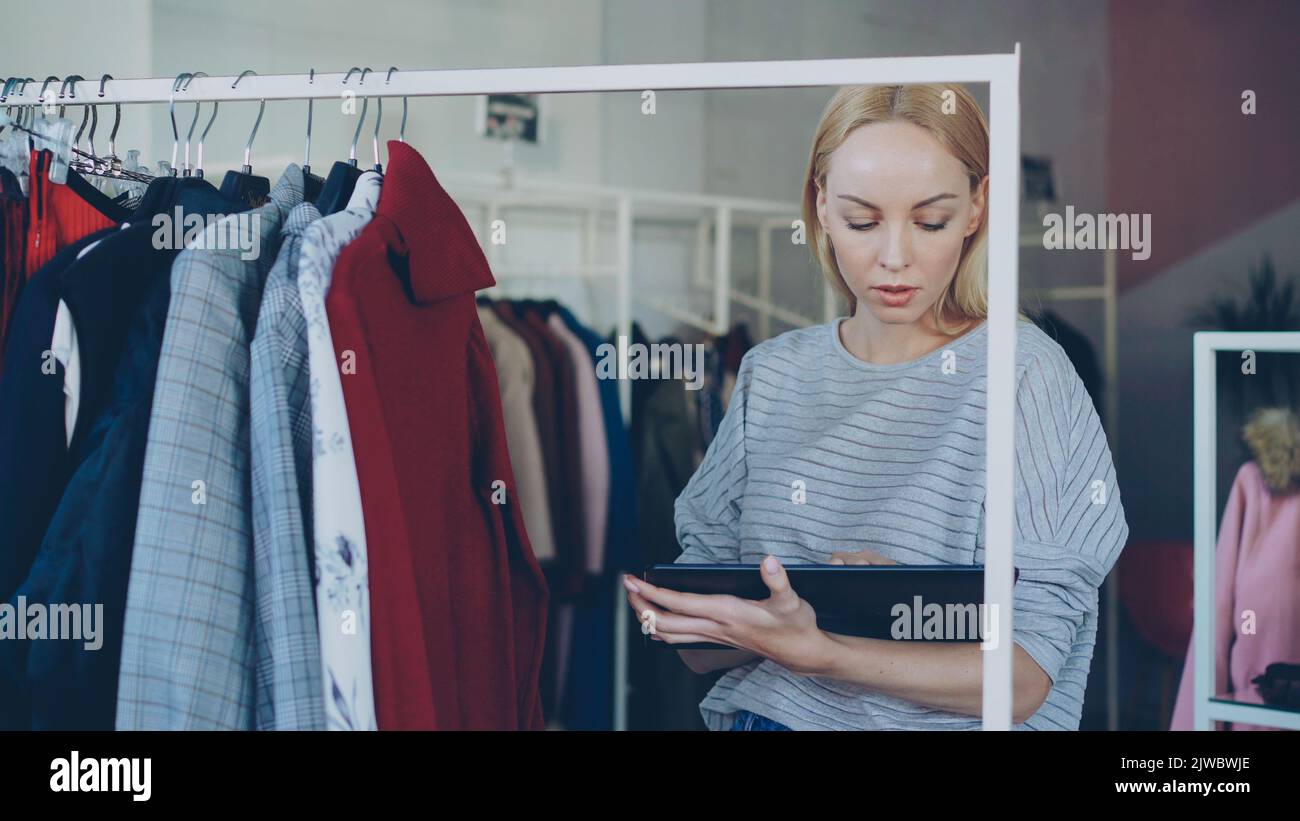 Young businesswoman is checking garments on rails and working with ... Young businesswoman is checking garments on rails and working with ...