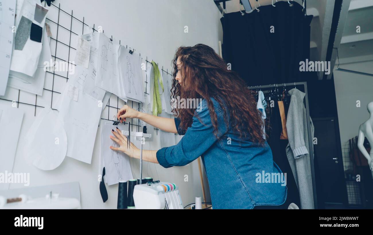 Low angle view of young attractive fashion designer looking at sketches ...