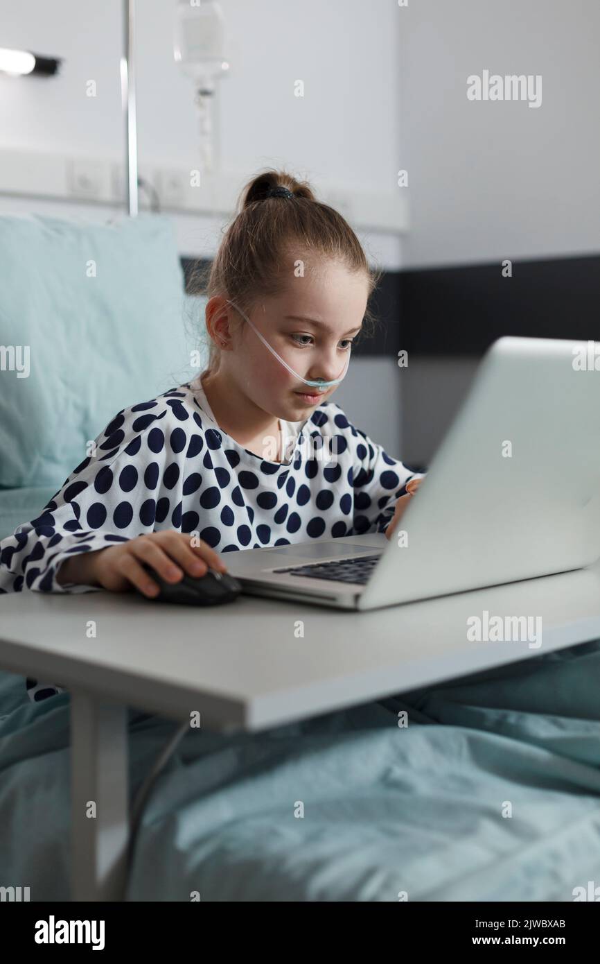 Ill kid resting on patient bed while enjoying gaming on modern computer ...