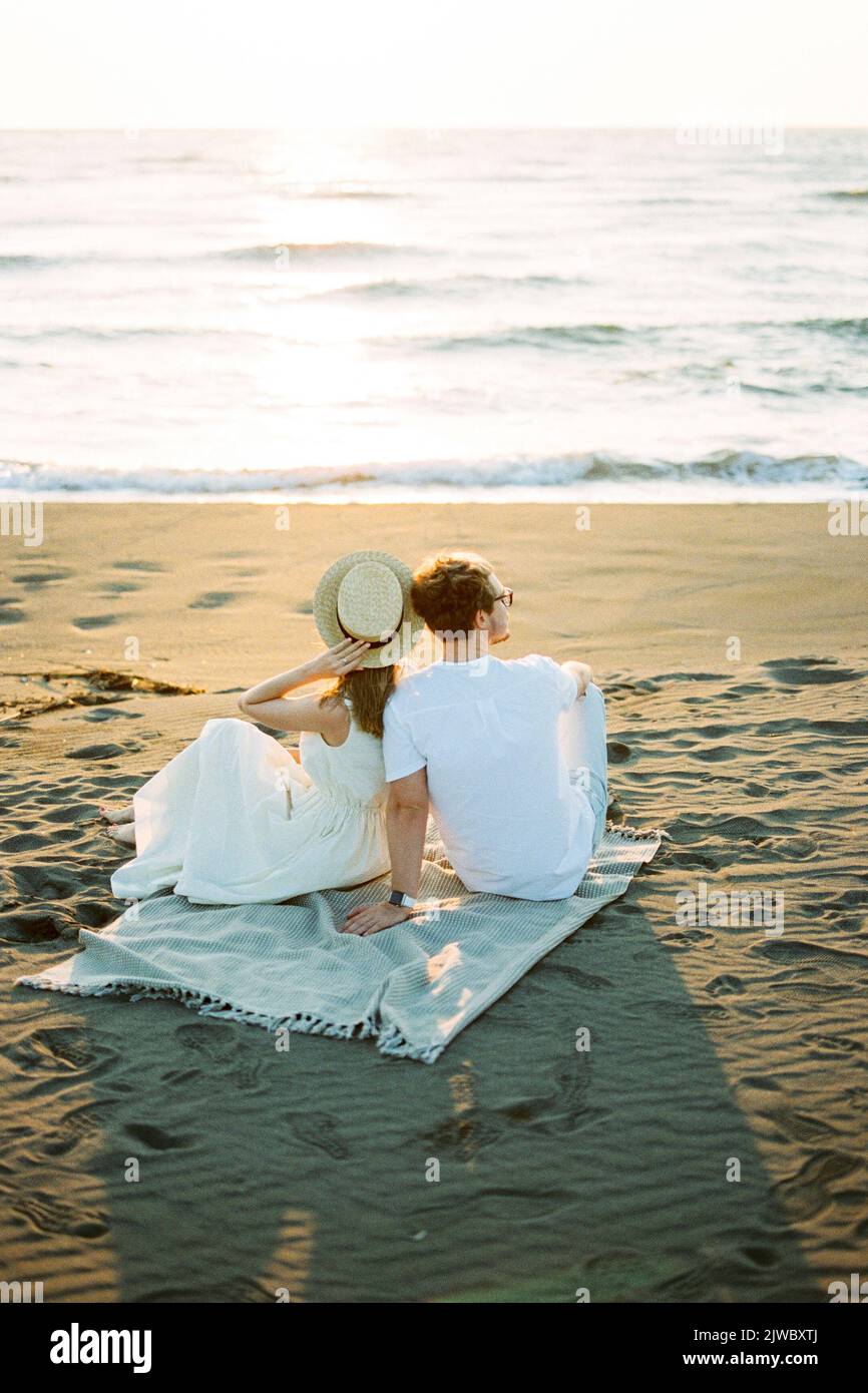 Woman in a hat sits on the beach leaning against the shoulder of a man ...