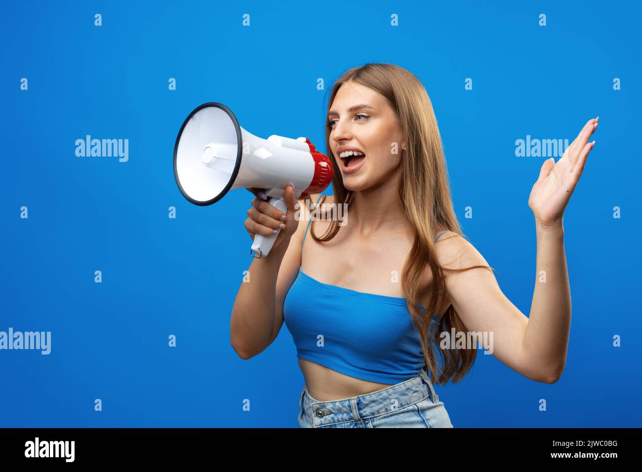 Young pretty woman with a megaphone against blue background in studio ...