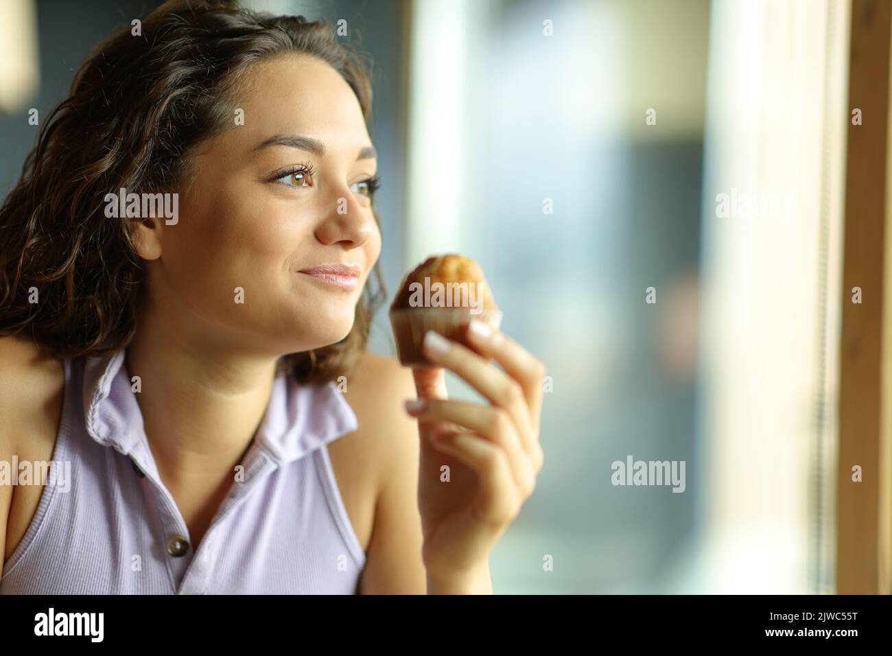 Happy woman holding a muffin in a restaurant and looking through a window Stock Photo - Alamy