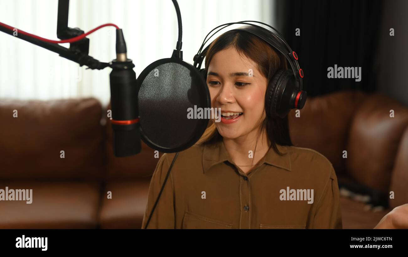 Pretty radio host wearing headphone and using condenser microphone ...