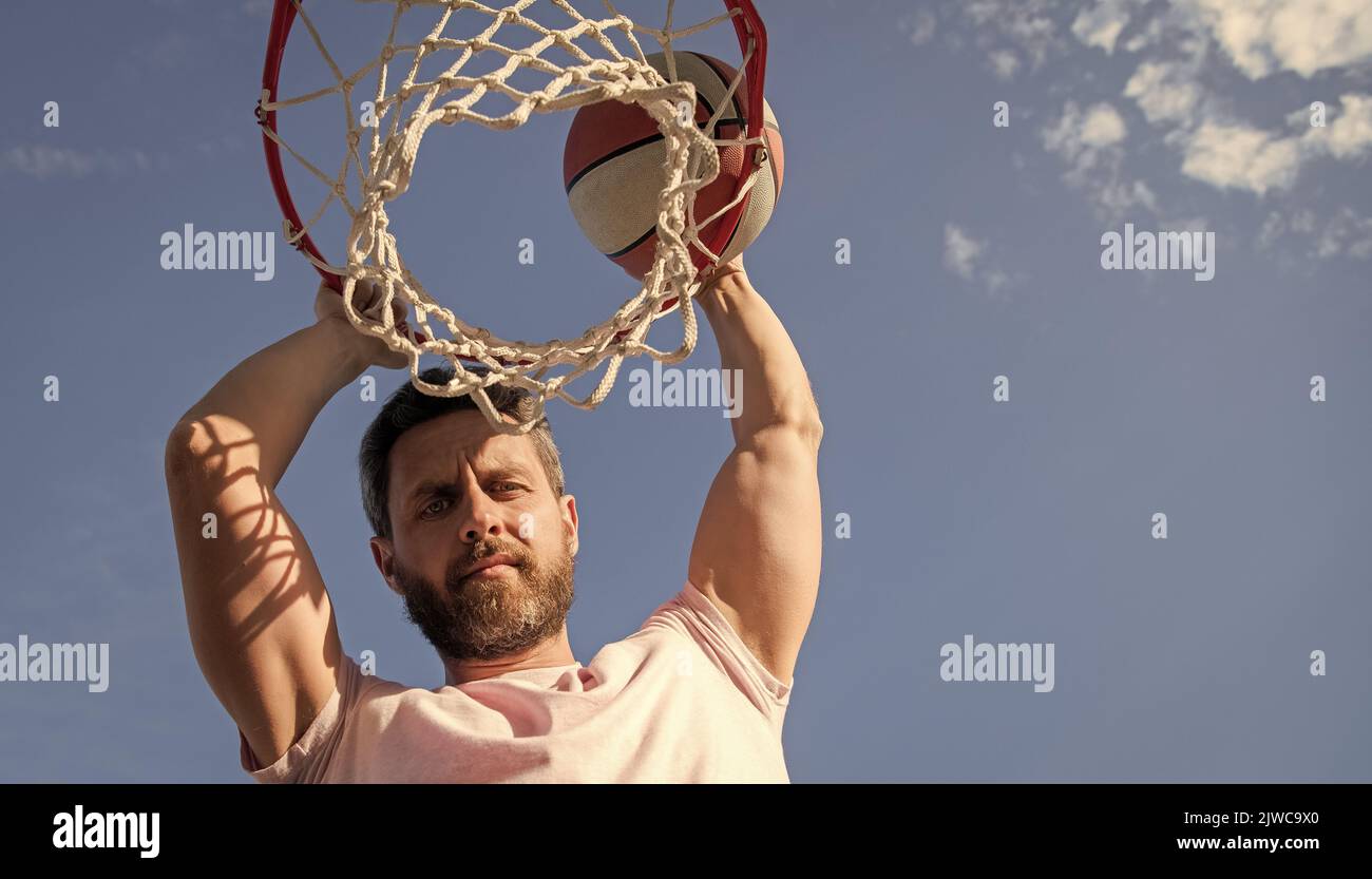 man dunking basketball ball through net ring with hands, copy space ...
